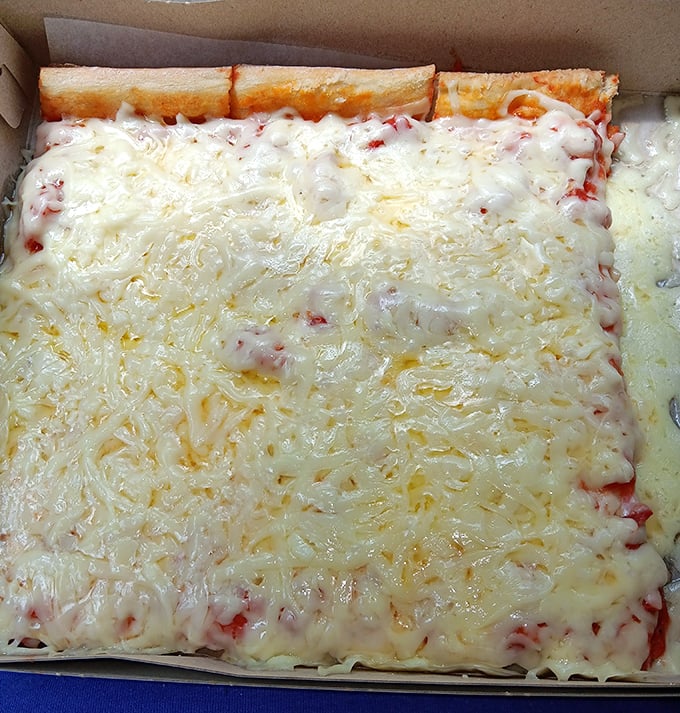 Behold the signature creation – a square canvas of hot crust and sauce adorned with a snowdrift of cold, shredded provolone that defies pizza physics.