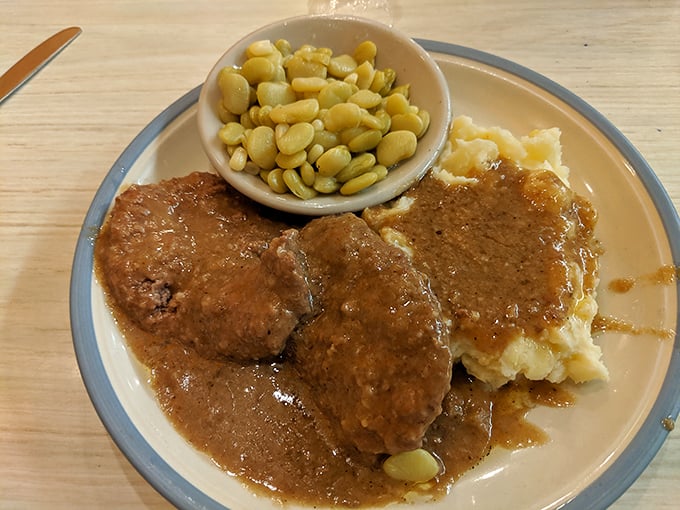 Behold the star attraction: country-style steak swimming in rich brown gravy alongside creamy mashed potatoes and lima beans—a holy trinity of Southern comfort.