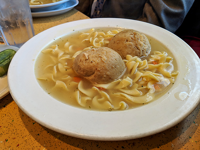 Behold the matzo ball soup—two perfect dumplings floating in golden broth like edible life preservers for your soul.