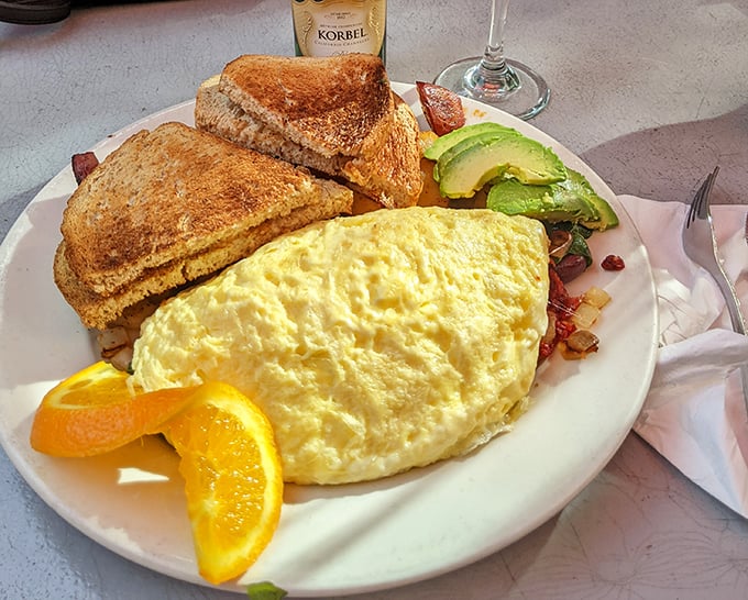 This omelet doesn't just sit on the plate—it lounges luxuriously, flanked by perfectly golden toast and avocado slices that California dreams are made of.
