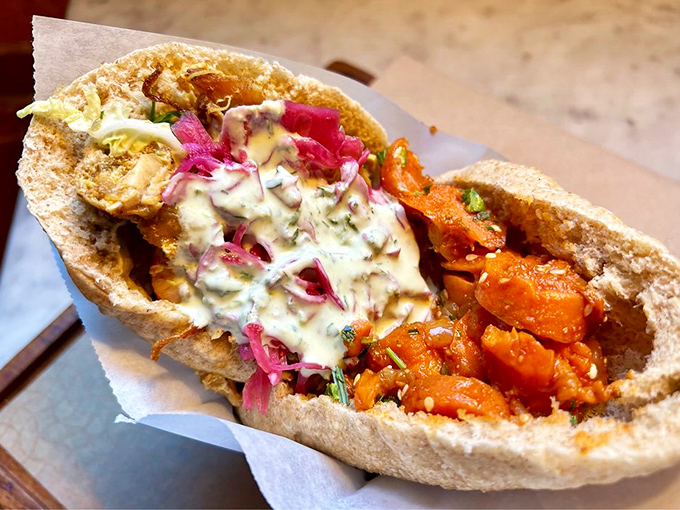 This isn't just a pita sandwich—it's an edible color wheel of vibrant pickled onions, roasted vegetables, and creamy sauce that makes your standard lunch weep with inadequacy.