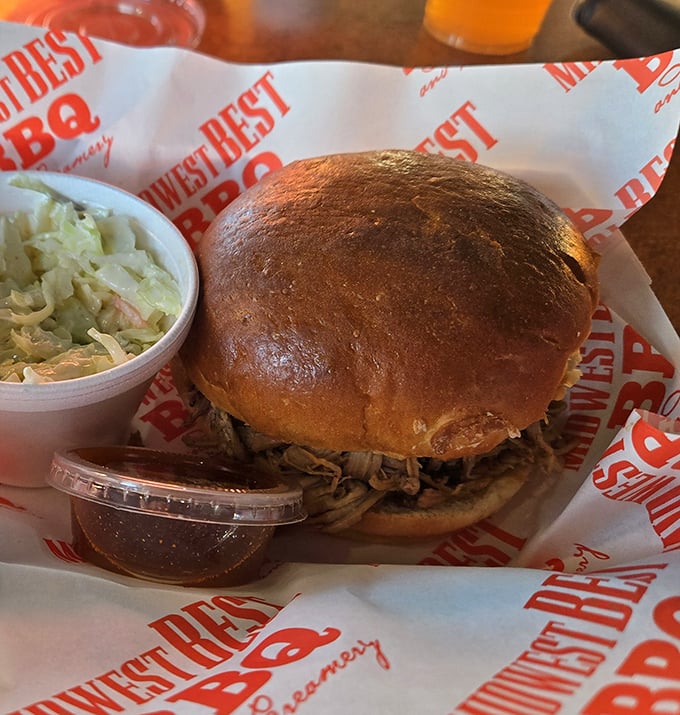 The pulled pork sandwich in its natural habitat – a golden-brown bun cradling a generous heap of smoky perfection with slaw standing by.