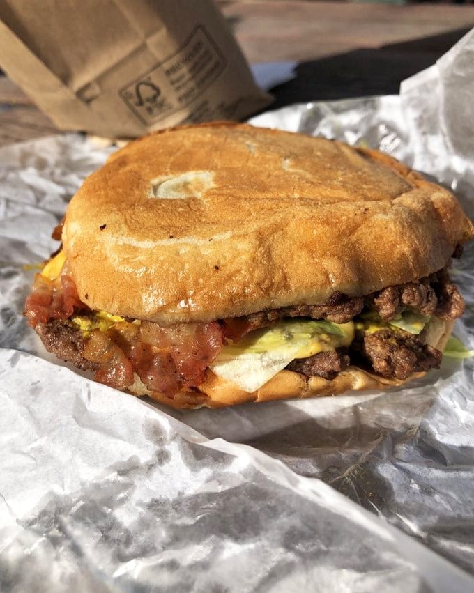 The bacon sandwich arrives wrapped in paper like a present, with that perfectly toasted bun cradling its contents like they're precious cargo—because they are.