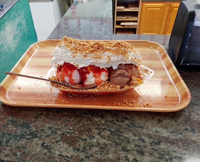 Behold the banana split—the architectural marvel of the dessert world. Graham cracker crumbs, whipped cream, and strategic berry placement create the perfect bite every time. 