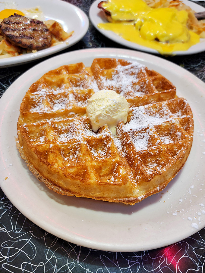 This golden waffle doesn't just wear its powdered sugar like a dusting of snow—it practically demands a moment of silent appreciation before diving in.