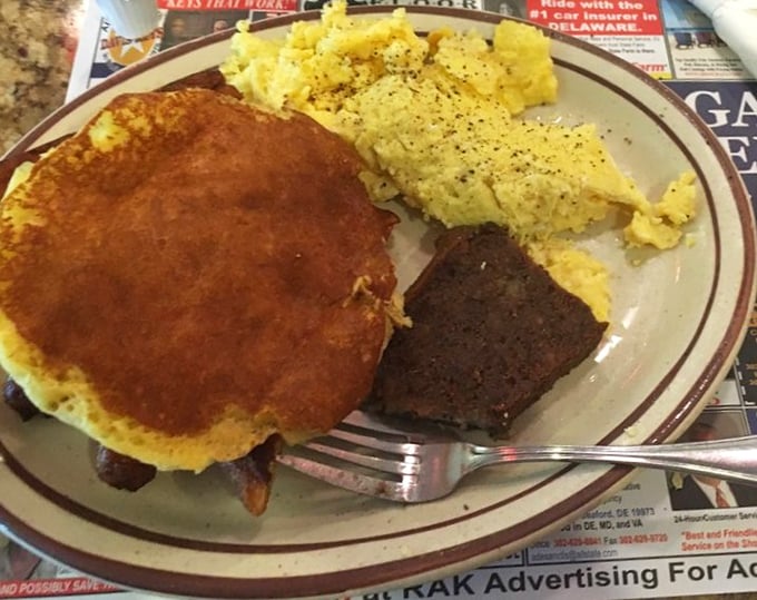 A hearty breakfast plate featuring a golden pancake, scrambled eggs, and scrapple – Delaware's morning trilogy of deliciousness that fuels the entire day.