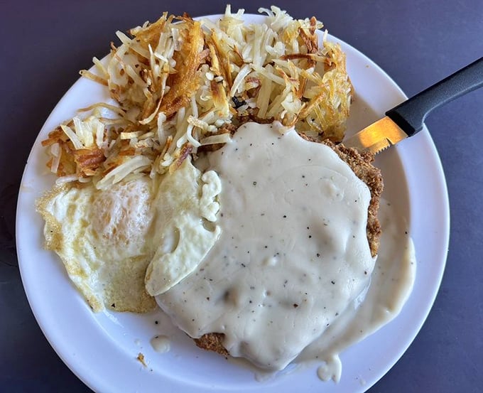 Chicken fried steak smothered in country gravy alongside crispy hash browns—the breakfast of champions and hangover heroes alike.