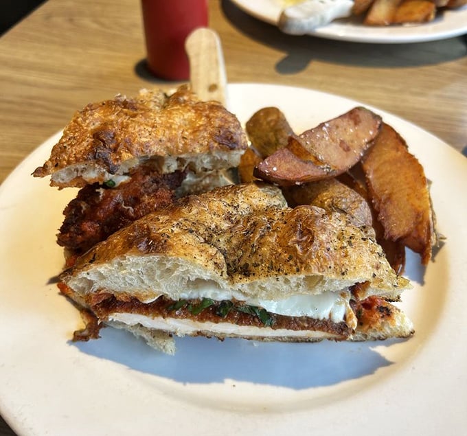 A sandwich that would make any Italian nonna proud—crispy chicken parmesan nestled between rustic bread with roasted potatoes standing guard.