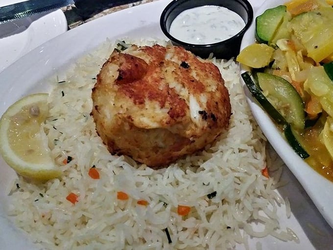 A perfect crab cake perched atop seasoned rice – no fillers, no nonsense. Just pure Maryland blue crab with a golden crust that shatters at the touch of a fork.