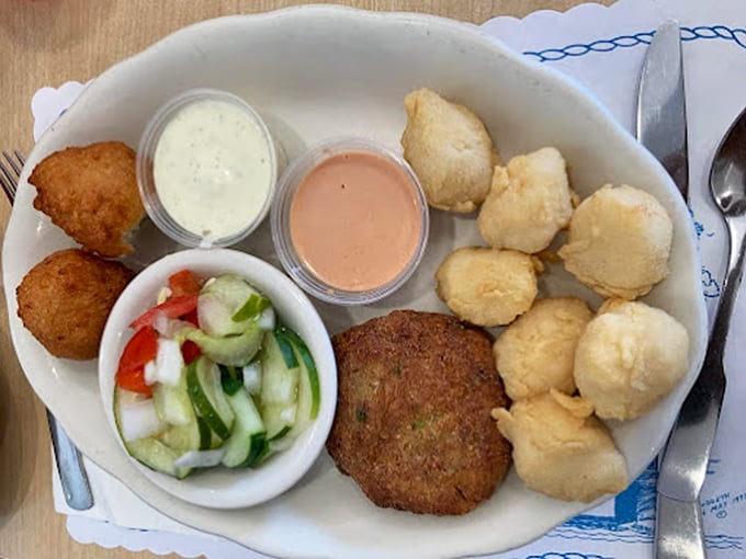 A seafood platter that makes you forget your table manners—hush puppies, crab cake, and cucumber salad creating the holy trinity of Southern sides.