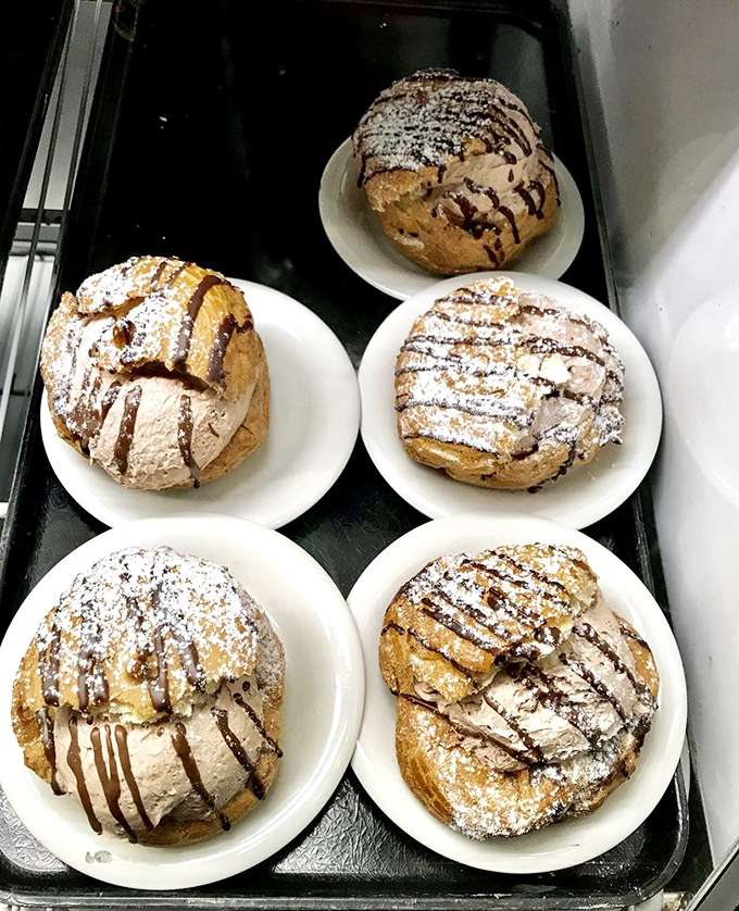 These cream puffs aren't just desserts, they're architectural achievements. The powdered sugar dusting is like fresh snow on the Alps of pastry perfection.