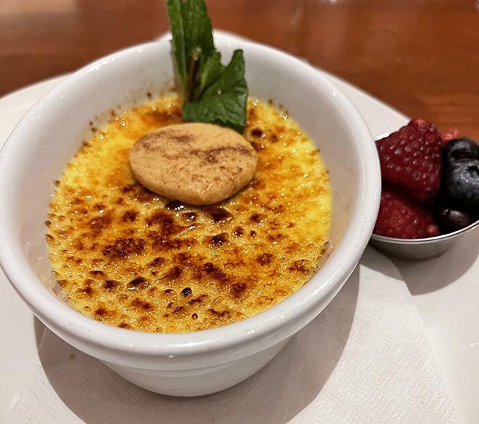Crème brûlée done right – that perfect crack of caramelized sugar revealing silky custard beneath, with berries standing by for moral support.