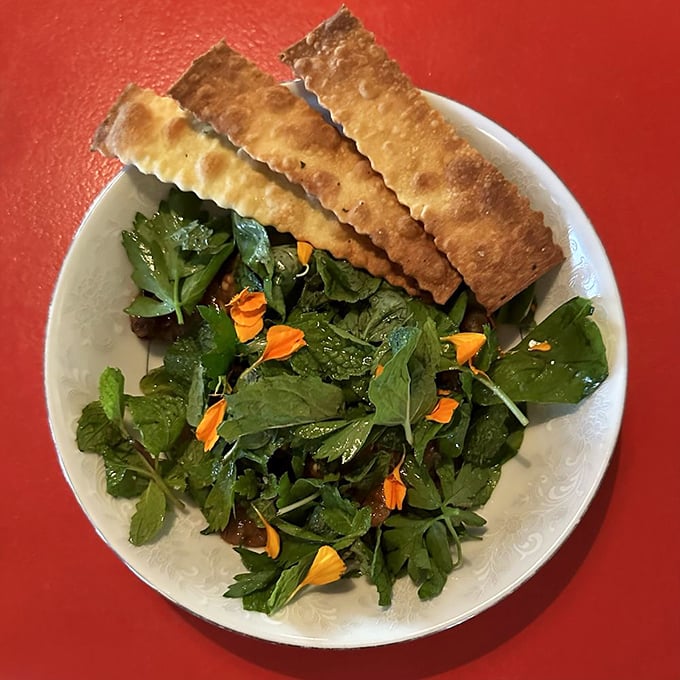Not your nonna's salad! Crisp greens, edible flowers, and housemade flatbread crackers create a garden on a plate that's almost too pretty to eat.