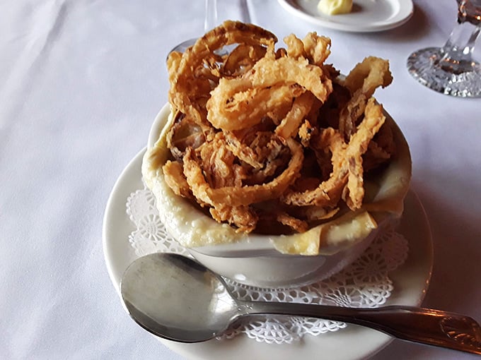 Behold the French onion soup in all its glory—a fortress of crispy onion straws defending a moat of savory broth that would make Julia Child weep with joy.
