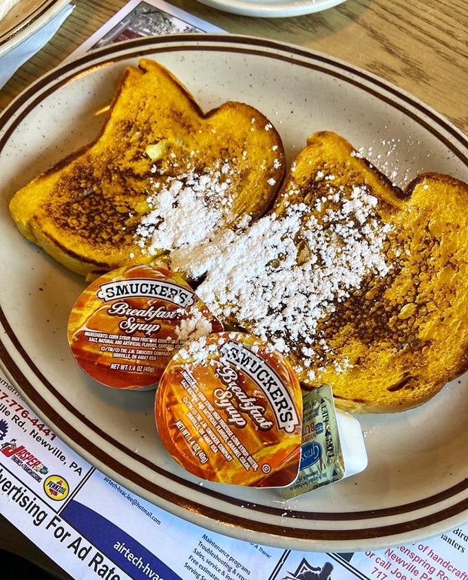 French toast dusted with powdered sugar like the first perfect snowfall of winter. Those Smucker's syrup packets—the universal language of American breakfast.