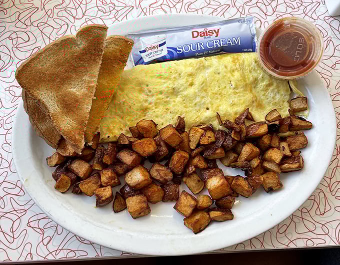 This omelet doesn't just sit on the plate—it commands it, flanked by an army of perfectly crisped home fries and toast standing at attention, ready for action.