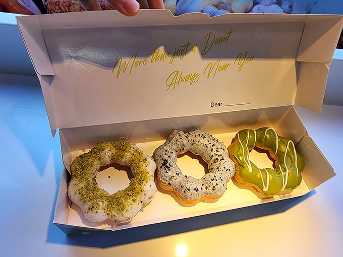 Three mochi donuts nestled in their box—one pistachio-dusted, one classic, one drizzled with white chocolate. Resistance is futile.