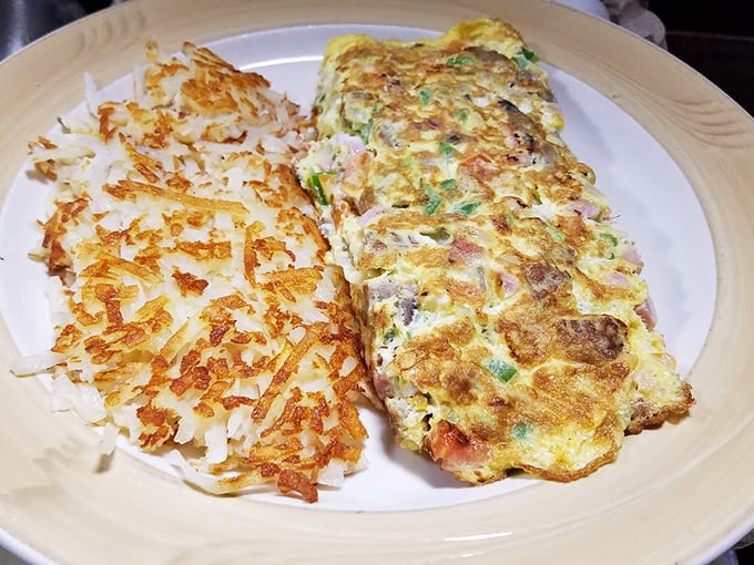 This omelet doesn't just sit on the plate—it commands attention with perfectly folded eggs alongside hash browns crisped to golden perfection.