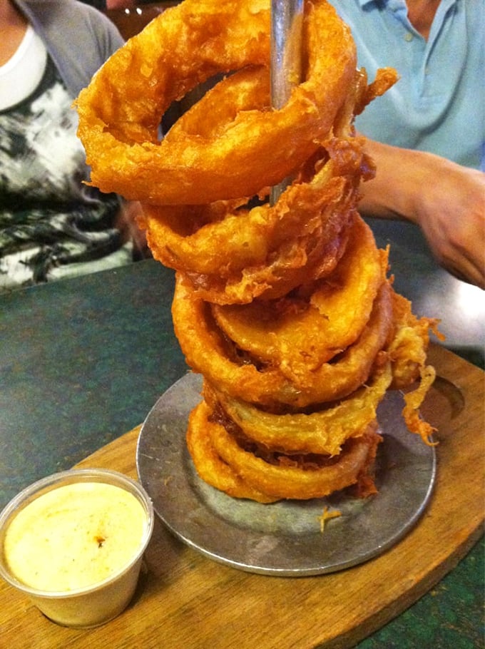 Onion rings stacked like golden Olympic rings—crispy, light, and the perfect vehicle for that creamy dipping sauce waiting patiently on the side.