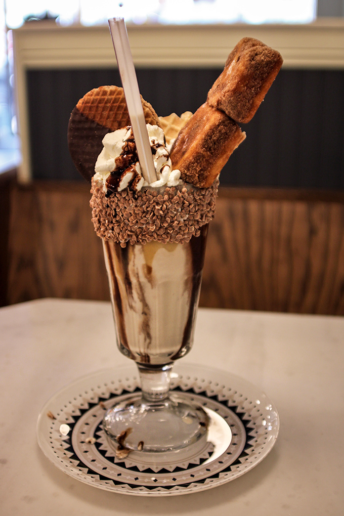 This isn't just a milkshake—it's an architectural marvel with chocolate, waffle pieces, and what appears to be churros standing guard over creamy perfection.