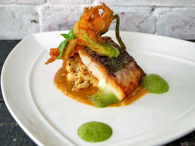 This isn't just fish – it's an artistic statement. Crispy-skinned bass perches atop a vibrant medley, garnished with a tempura-fried squash blossom.