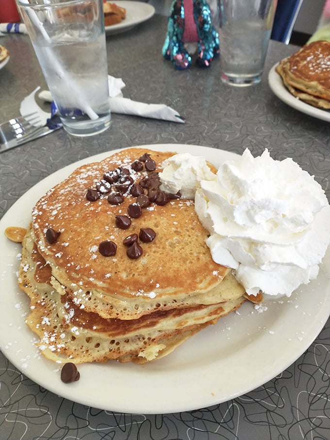 These aren't just pancakes—they're fluffy discs of joy, wearing chocolate chips like medals of honor and crowned with whipped cream royalty.