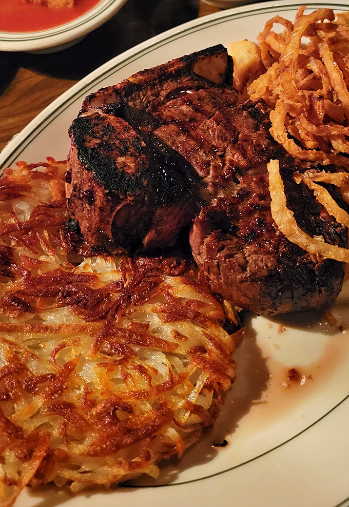 The porterhouse arrives like a challenge – gloriously charred exterior, tender interior, and those crispy hash browns that might steal the show.