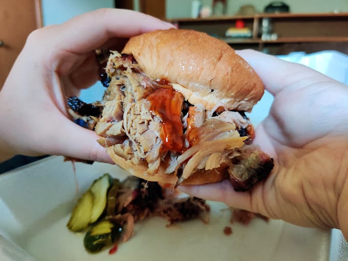 This pulled pork sandwich isn't just a meal—it's an architectural marvel of tender meat and sauce that requires both hands and absolutely zero dignity to consume properly.