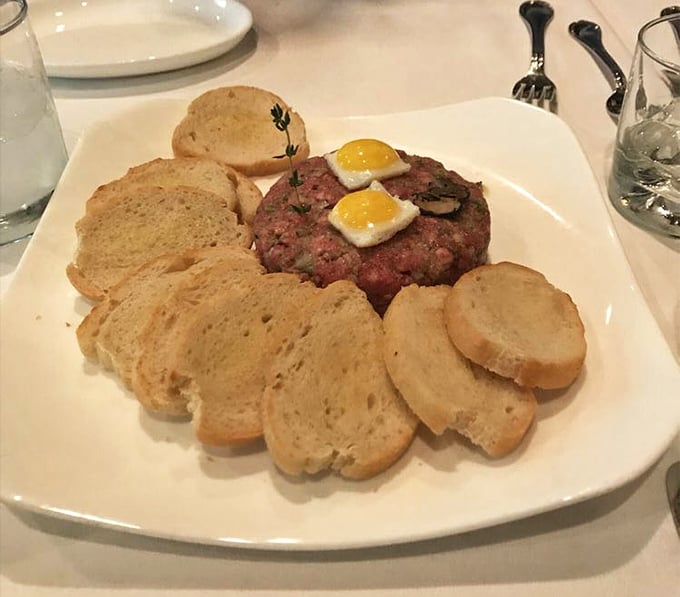 Steak tartare presented with military precision—raw beef never looked so civilized, topped with tiny sunny-side up quail eggs like culinary jewelry.