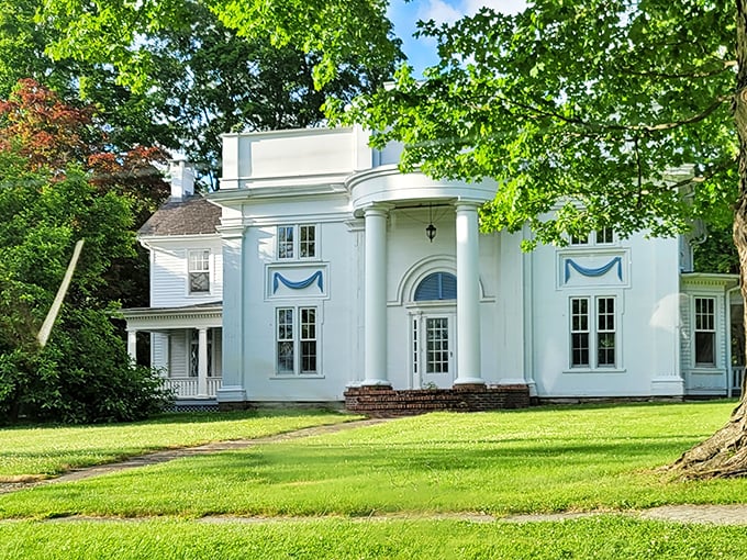 This elegant white mansion whispers stories of history while standing proudly among towering shade trees.
