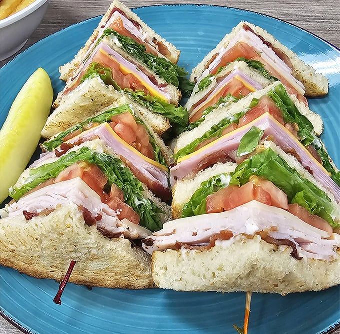 This club sandwich isn't just stacked—it's architected. The Empire State Building of lunch options, complete with a pickle skyline.