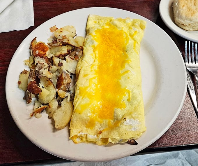 This isn't just an omelet—it's breakfast architecture, with perfectly folded eggs cradling melted cheese alongside home fries that deserve their own zip code.