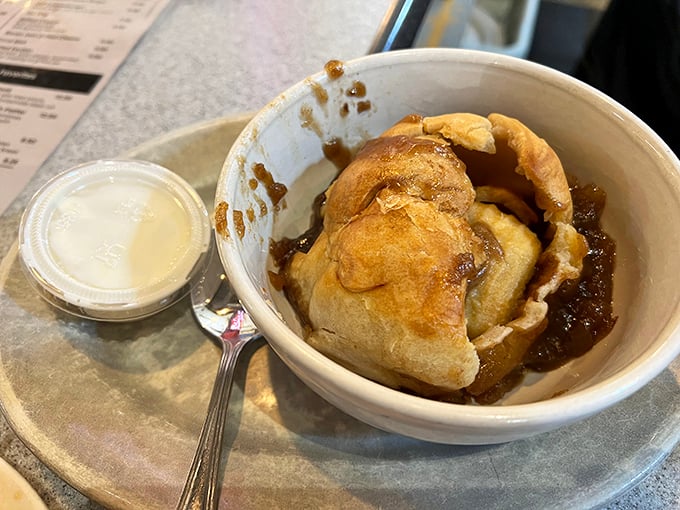 The legendary apple dumpling in all its glory—a whole apple wrapped in flaky pastry, swimming in cinnamon-spiced syrup with cream on the side.