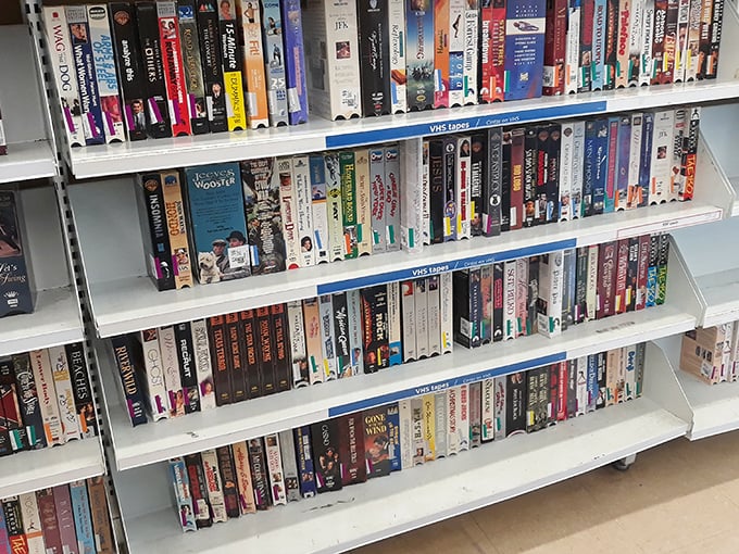 VHS tapes stand like ancient artifacts from a bygone era. "Be Kind, Rewind" – instructions as quaint as rotary phones.
