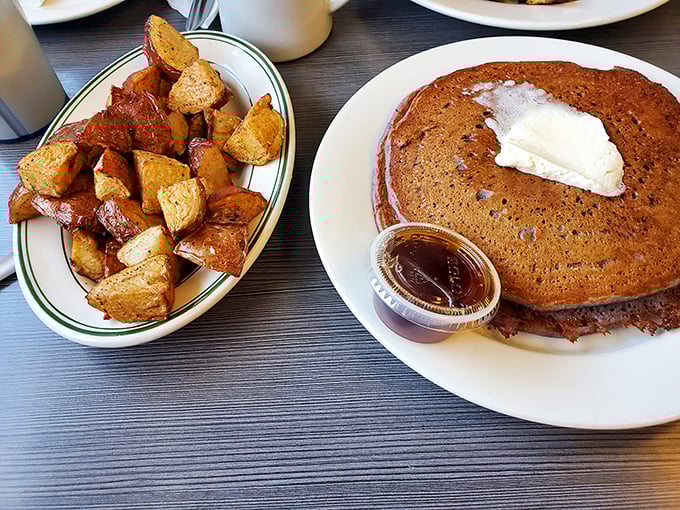 A pancake with a pat of butter melting into its warm embrace, alongside crispy home fries—this isn't just breakfast, it's morning therapy.