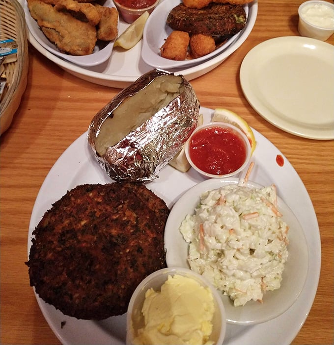 This isn't just a crab cake—it's a golden-brown disk of maritime perfection, keeping company with creamy coleslaw and a baked potato in foil.