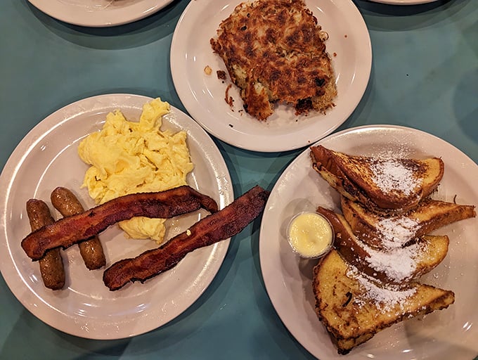 The holy trinity of breakfast perfection—golden scrambled eggs, sausage links with that satisfying snap, and French toast dusted with powdered sugar that'll make you forget your diet resolutions.