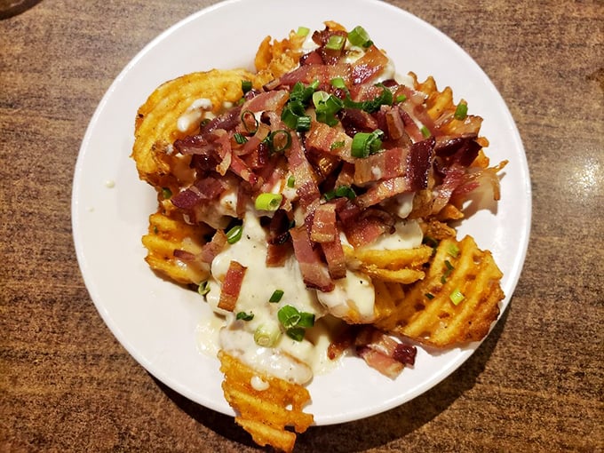 The infamous pork poutine in all its glory—waffle fries buried under an avalanche of bacon, cheese, and gravy that would make a Canadian weep with joy.