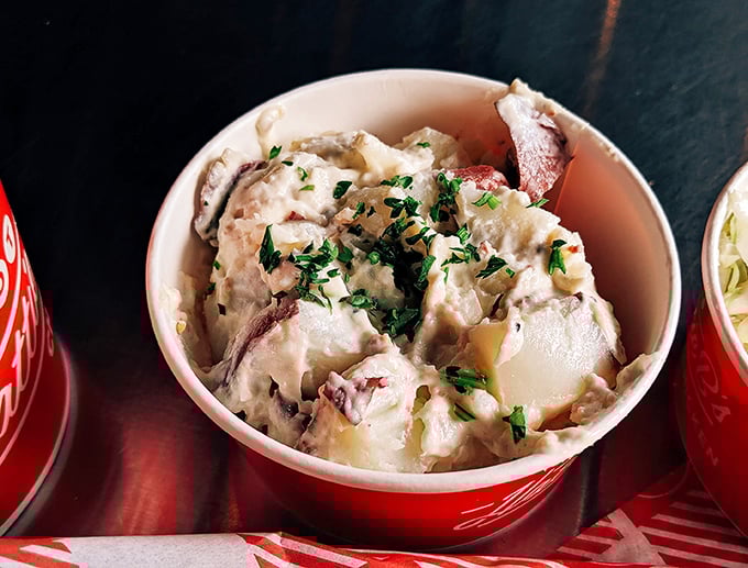 Creamy potato salad in its red-rimmed cup isn't just a side—it's the cooling diplomat negotiating peace between your taste buds and that fiery chicken.
