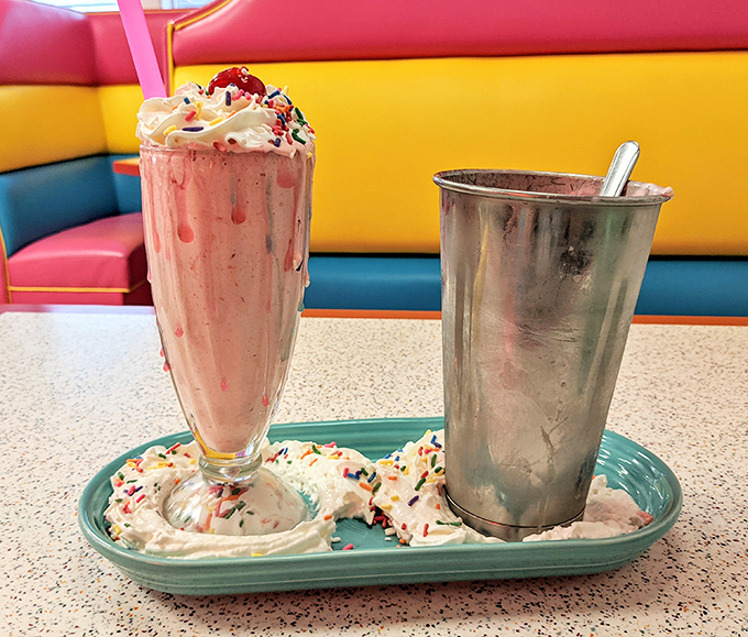 Pink perfection in a glass! This strawberry milkshake wears its whipped cream crown and sprinkles like royalty, while the metal mixing cup offers bonus sips—like finding an extra $20 in your pocket.