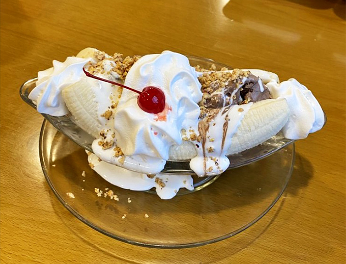 The banana split arrives like a cloud formation—peaks of whipped cream, valleys of ice cream, and that signature cherry summit. 
