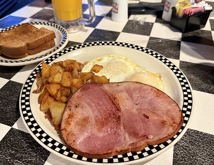 The classic breakfast trinity: eggs, ham, and home fries, served on the signature checkered-rim plates that frame every delicious meal here.