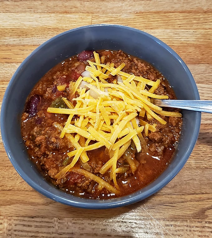 A bowl of chili topped with melted cheddar—the kind that makes you wonder if grandmothers secretly run the kitchen here.