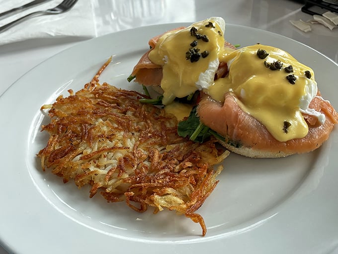 Eggs Benedict elevated to an art form—perfectly poached eggs nestled on salmon, draped in hollandaise that's sunshine on a plate, with crispy hash browns standing guard.
