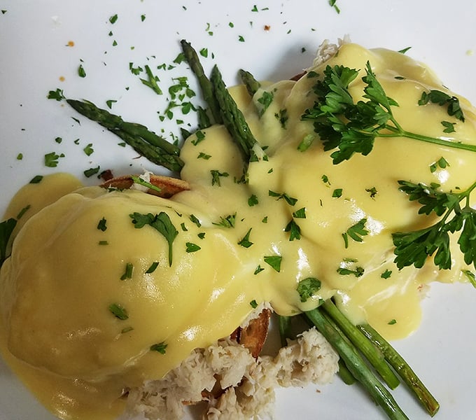 Hollandaise sauce cascading over asparagus like a yellow waterfall of buttery goodness. This eggs benedict isn't just breakfast—it's an event.