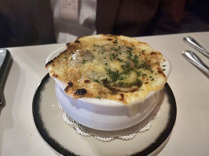 The French onion soup arrives with a crown of melted cheese that stretches dramatically, revealing a rich broth beneath.
