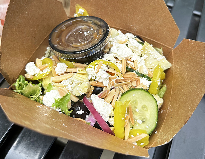 A Mediterranean salad that actually looks like someone cares—fresh vegetables, feta, and almonds nestled in a compostable container that says "we're trying here."