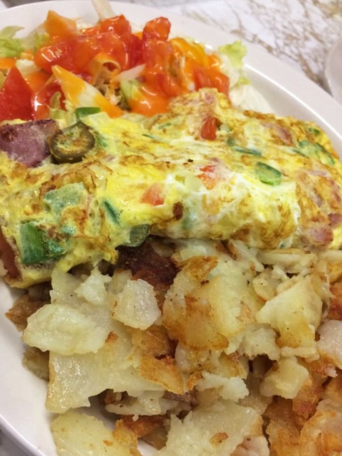 Breakfast alchemy at its finest—an omelet packed with veggies and meat, alongside potatoes crisped to golden perfection on a well-seasoned grill.