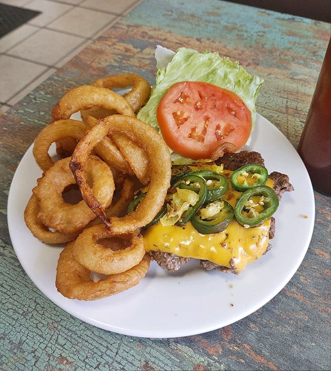 Golden onion rings frame a burger topped with melty cheese and jalapeños. A symphony of crunch, spice, and satisfaction on a classic white plate.
