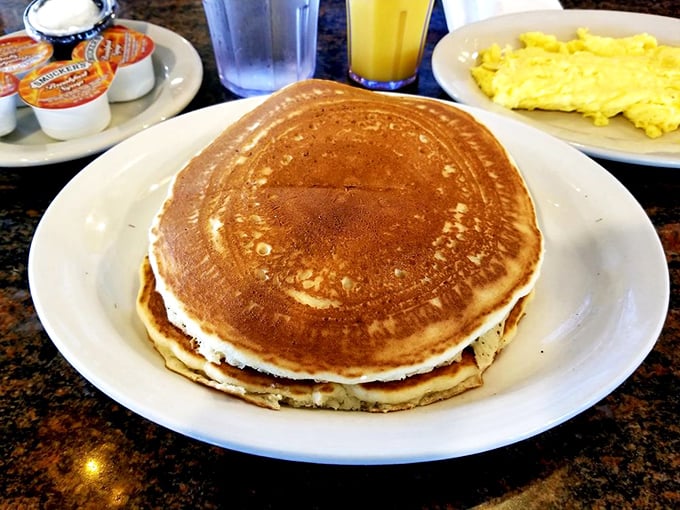 Pancake perfection doesn't need to whisper—it speaks for itself. Golden, fluffy discs ready for their maple syrup baptism alongside eggs for the complete breakfast experience.